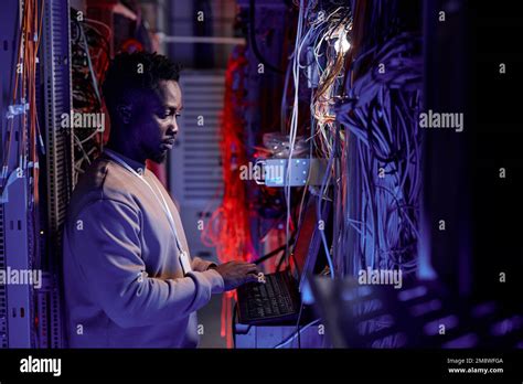 Side View Portrait System Administrator Using Computer In Server Room Lit By Neon Light Stock