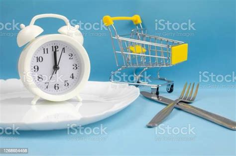 흰색 알람 시계는 포크와 칼 쇼핑 카트 클로즈업과 파란색 배경에 흰색 접시에 서있다 저녁 식사 창조적 인 시간의 개념 0명에 대한 스톡 사진 및 기타 이미지 Istock