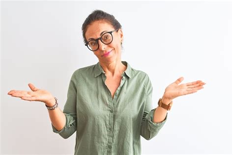 녹색 셔츠와 안경을 쓰고 고립된 흰색 배경 위에 서있는 중년 여성은 팔과 손을 들고 혼란스러운 표정을 짓고 있습니다 의심 개념 한 명의 여자만에 대한 스톡 사진 및 기타