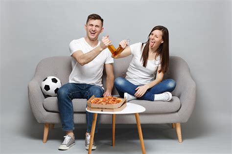 웃 고 있는 커플 여자 남자 축구 팬 응원 좋아하는 팀 혀를 보여주는 회색 벽 배경에 고립 된 맥주 병 보유 사람들의 감정