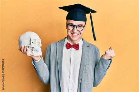 Young Caucasian Nerd Man Wearing Glasses And Graduation Cap Holding Skull Screaming Proud
