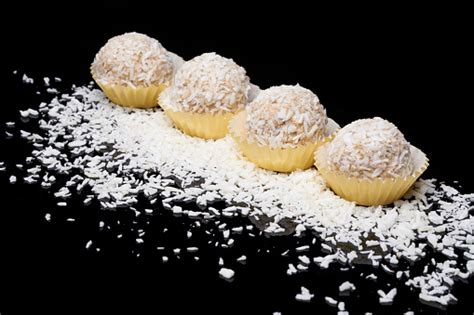 검은 유리 배경에 흰색 코코넛 공 원시 및 건강한 무설탕 라파엘로 사탕 코코넛 조각에 공을 덮고 비건 채식과자 가루로 빻은에