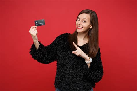 신용 은행 카드 스튜디오에서 밝은 빨간 벽 배경에 고립에 검은 모피 스웨터 포인팅 검지 손가락에 매력적인 젊은 여자 사람들이 진심으 감정 라이프 스타일 개념 복사 공간을