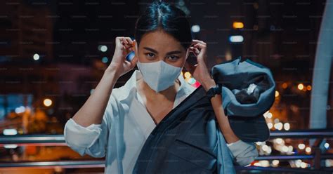 패션 사무복을 입은 성공적인 젊은 아시아 사업가는 의료용 안면 마스크를 쓰고 웃으며 카메라를 바라보며 도시의 현대 도시의 밤에 야외에서 혼자 서 있습니다 이동 중 비즈니스