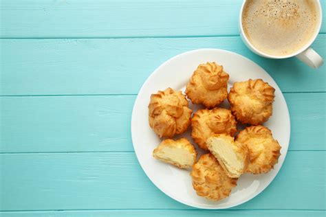 파란 나무 배경에 커피 한 잔과 함께 접시에 크림을 곁들인 수제 수익 창출 갓 구운 황금 프로피테롤 갈색에 대한 스톡 사진 및