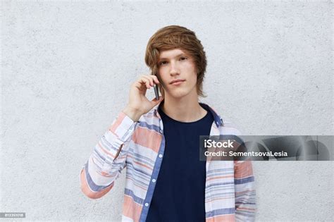 어두운 눈과 심각한 식 스마트 전화를 통해 그의 어머니를 호출 하는 데 세련 된 헤어스타일 Hipster 소년 흰 콘크리트 벽에 고립 세련 된 십 대 그의 친구와 함께 채팅