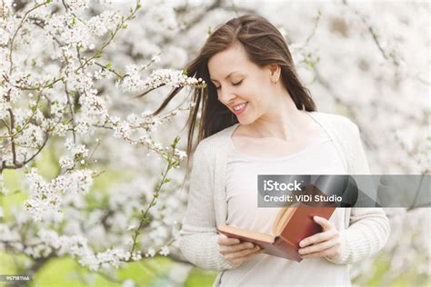 편안한 미소 영 부드러운 여자 시 정원이 나 공원 피 나무 배경에 흥미로운 책 서를 읽고 가벼운 캐주얼 옷에 봄 자연 꽃입니다 라이프 스타일 레저 개념 고름에 대한 스톡