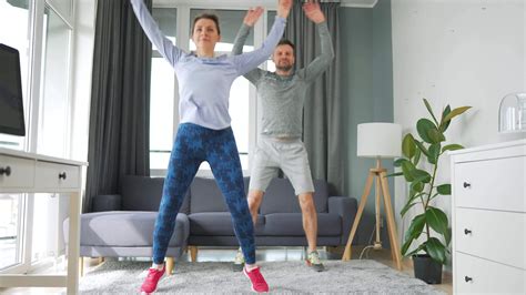 Caucasian Couple Is Doing Jumping Jacks Exercise At Home In Cozy Bright