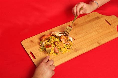 사프란 조개류 새우 야채로 만든 발렌시아 스페인의 전통 빠에야 쌀은 나무 판에 담겨 있고 흰색 배경에 포크를 가져 오는 손 0