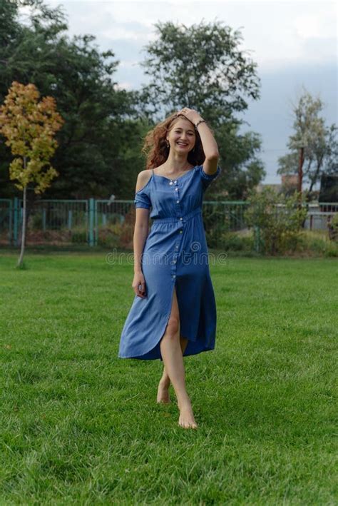 Молодая женщина в синем платье ходит босиком по траве в парке Стоковое Изображение изображение