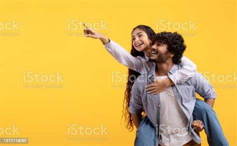 흥분 젊은 인도 부부 데 재미 와 레이디 피기 백 남자 와 가리키는 손가락 에 여유 공간 에 노란색 배경 2명에 대한 스톡 사진 및 기타 이미지 Istock