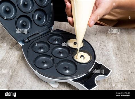A Person Is Making Donuts In A Donut Maker The Donuts Are Being Filled With A White Glaze Stock