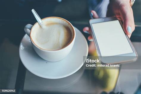 카페에서 커피를 마시는 동안 빈 데스크톱 화면과 흰색 휴대 전화를 들고 여자의 손의 상위 보기 이랑 이미지 공란에 대한 스톡