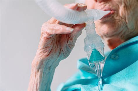 낮은 각도 닫기 블루 액체 약물의 샷 으로 수석 백인 여자 앉아 집에서 호흡 분무기를 사용 하 여 천식을 치료 하거나 폐 기도를 열고 약물을 흡입 네블라이저에 대한 스톡