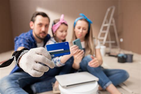 새 아파트에서 시간을 보내는 아이와 사랑에 빠진 젊은 부부 방 그림 벽 가족 온라인 쇼핑을 위해 신용 카드로 가구 지불 주문에 대한 영감을 탐색 Diy에 대한 스톡 사진 및