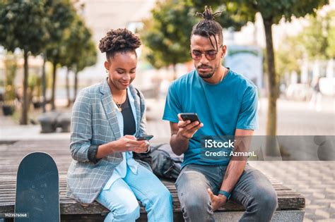귀여운 젊은 흑인 커플 야외에 앉아 그들의 스마트 폰을 사용하여 20 24세에 대한 스톡 사진 및 기타 이미지 20 24세