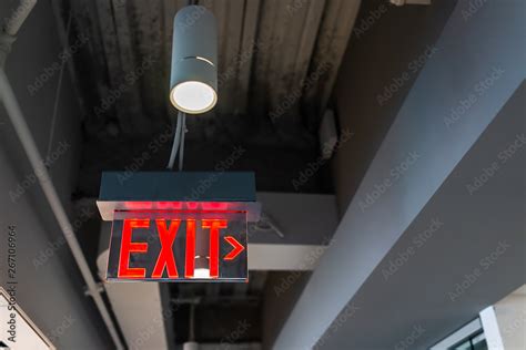 Red Exit Sign Hanging From Ceiling Looking Up View With Arrow Direction And Color Illuminated