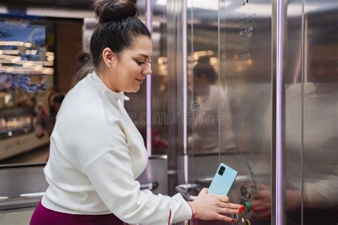 woman pressing elevator button while using smartphone in a mall stock
