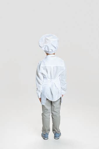 흰색 요리사 유니폼을 입은 어린 소년과 흰색 스튜디오 배경에 고립된 거대한 요리사의 모자를 입은 어린 소년의 뒷모습 6 7 살에 대한 스톡 사진 및 기타 이미지 Istock
