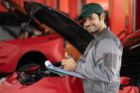 자동차 정비사 남자는 클립 보드를 들고 엄지 손가락을 들고 카메라를 보며 자동차 손상 깨진 부품 상태를 확인하는 미소를 짓고