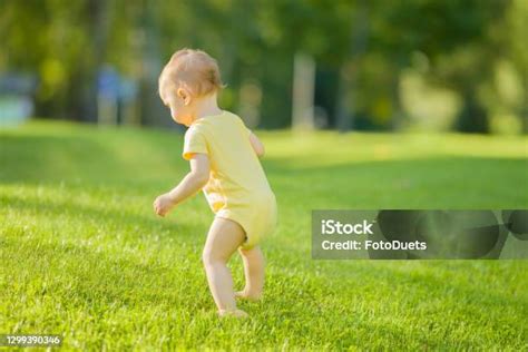 노란 바디수트를 입은 아기 소녀는 따뜻한 화창한 여름 날에 신선하고 녹색 잔디에 맨발로 달려 있습니다 측면 보기입니다 외부 첫 번째 단계 걷기에 대한 스톡 사진 및 기타