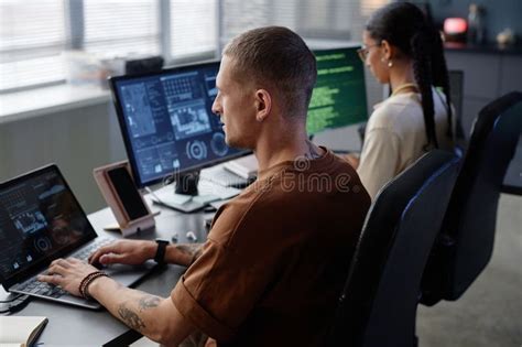 side view of male it programmer with earring coding on laptop at