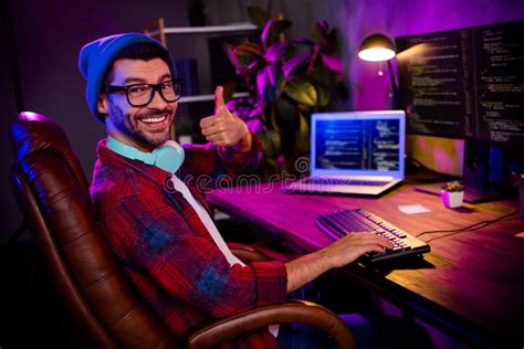 Photo Of Confident Smiling Coder Dressed Hat Eyewear Showing Thumb Up Working Modern Gadget