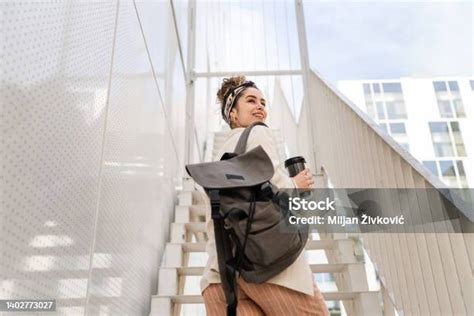 한 여성 젊은 성인 백인 여학생 배낭을 들고 서서 종이와 커피 한 잔을 들고 대학 건물 앞에서 밝은 날의 행복한 미소를 지으며 실제 사람들이 공간을 복사합니다 건물 외관에