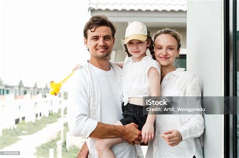 여름 복장을 입고 발코니에서 좋은 시간을 보내는 행복한 혼혈 가족 3 명 미소 짓는 부모는 어린 딸을 안고 사랑 다양성 유대감을 자연광에 담습니다 25 29세에 대한 스톡