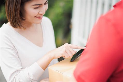 젊은 아시아 여자 디지털 사인 기술 스마트폰 수신 소포 골판지 상자 에서 포스트 남자 집 아웃도어에서 미소와 벌채 행복 배달 남자 익스프레스 배송 상품 고객에 게 고객에