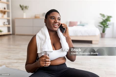 홈 스포츠 훈련에서 휴식에 스마트 폰에 말하는 물 유리와 과체중 흑인 여성 Brand Name Smart Phone에 대한 스톡 사진 및 기타 이미지 Brand Name