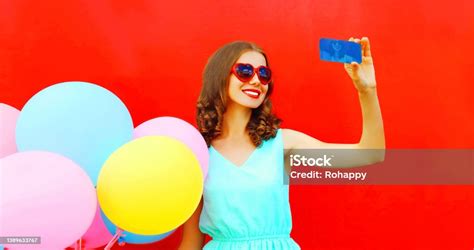 빨간색 배경에 화려한 풍선으로 스마트 폰으로 셀카를 찍는 행복한 웃는 여성의 초상화 여름에 대한 스톡 사진 및 기타 이미지 여름 휴대전화 25 29세 Istock