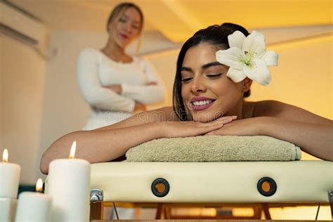Gorgeous European Girl With Flower In Her Hair Posing On Massage Table Masseuse In Background