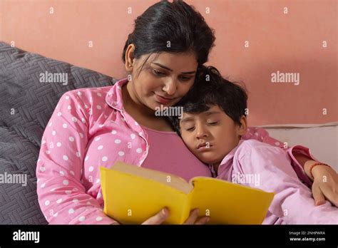 Mother Putting Her Son To Sleep While Reading A Book On Bed Stock Photo Alamy