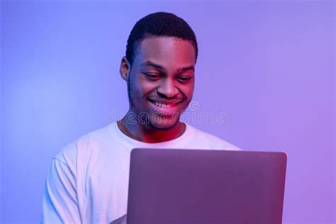 Handsome Smiling Black Programmer Guy Working Online On Laptop In Neon