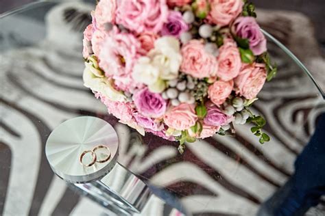 두 개의 황금 고리와 분홍색과 보라색 장미의 무성한 신부 꽃다발을 실내에서 유리 테이블 배경에 흐릿하게 닫습니다 선택적 초점 웨딩 컨셉 0명에 대한 스톡 사진 및 기타