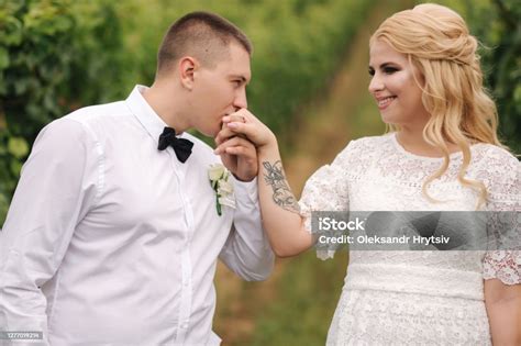 신랑과 신부는 결혼식 날에 포도원에서 걷고 있습니다 금발의 머리 여자는 흰색 드레스에 손에 결혼식 꽃다발을 개최 신랑 키스 신부의 손 로맨스에 대한 스톡 사진 및 기타