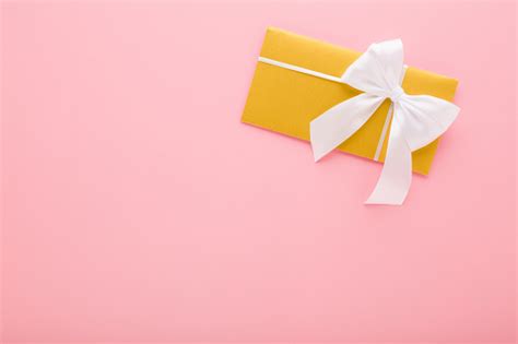 밝은 분홍색 테이블 배경에 흰색 리본이 있는 닫힌 황금 결혼식 봉투 파스텔 색상 근접 촬영 영감을 주는 텍스트 사랑스러운 인용문