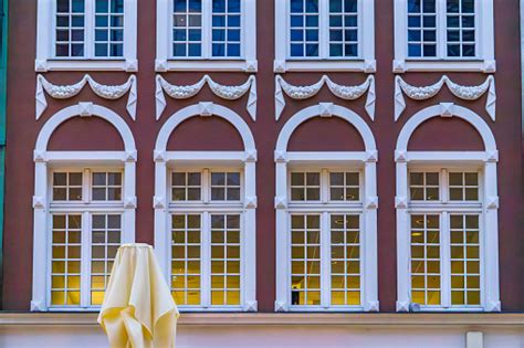 흰색 치장 벽토 장식으로 장식 된 높고 우아한 창문이 줄지어 있는 유서 깊은 타운 하우스의 외관입니다 건물은 짙은 붉은색의 외관과 화환 아치와 같은 고전적인 장식이