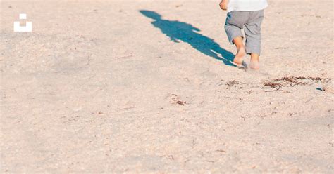 흰색 티셔츠와 갈색 반바지를 입은 소년이 수역 근처의 갈색 모래 위에 서 있다 사진 Unsplash의 무료 벽지 이미지