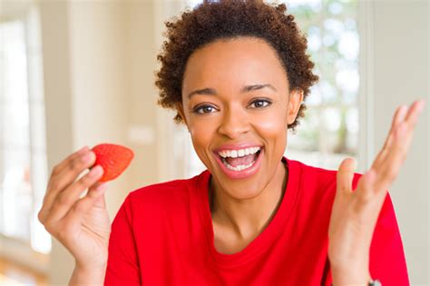 아침 식사를 위해 신선한 딸기를 먹는 젊은 아프리카 계 미국인 여성은 매우 행복하고 흥분 큰 미소와 손을 들고 비명을 지르는 승리를 축하하는 우승자 표정 건강한 생활방식에