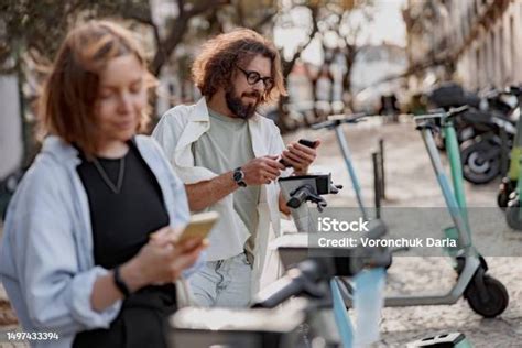 부부는 도시의 거리에 서서 휴대 전화를 사용하여 전기 푸시 스쿠터를 대여합니다 2명에 대한 스톡 사진 및 기타 이미지 2명