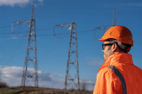 Construction Worker Surveys Electrical Infrastructure With Electrical Pylons Blue Sky