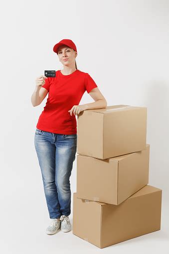 전체 길이 빨간 모자에 배달 여자의 초상화 T셔츠는 흰색 배경에 고립 신용 카드 빈 골 판지 상자 근처 여성 택배 수신 패키지입니다 광고에 대 한 공간을 복사 합니다