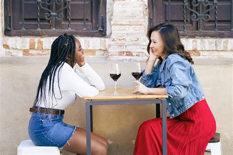 두 명의 다민족 친구가 술집 밖의 테이블에 앉아 레드 와인 한 잔을 마시면서 이야기합니다 18 19세에 대한 스톡 사진 및 기타 이미지 18 19세 25 29세 2명
