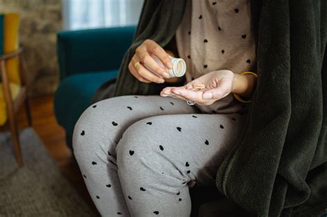 감기 발열 두통 및 독감 증상 담요로 덮인 아픈 여자가 거실 소파에 앉아 약을 먹고 있습니다 계절성 호흡기 질환 테이블 위에 온도계 알약 비타민 물 한 잔이 놓여 있습니다