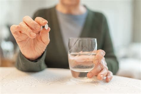 약을 먹기 위해 알약과 물 한 잔을 들고 있는 노인 여성의 클로즈업 노화 건강 관리 및 치료의 개념 노인을 위한 의약품 처방약의 책임감 있는 사용 80 89세에 대한 스톡