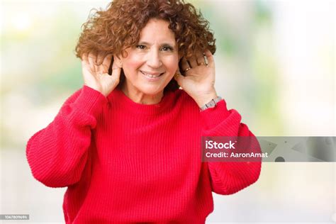 아름 다운 중간 어른 둘 다 들 려 고립 된 배경 위에 빨간 고위 여자 겨울 스웨터 귀 제스처가 십에 대 한 호기심에 손 청력 문제 청각 갈색 머리에 대한 스톡 사진 및