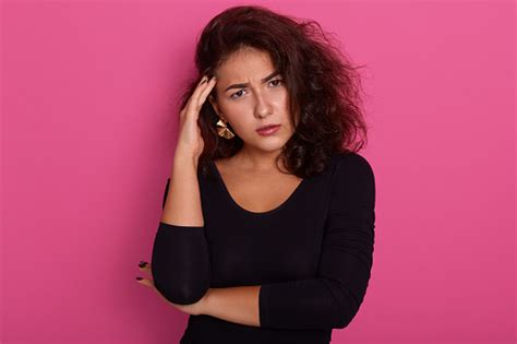 사원에 그녀의 검지 손가락을 들고 어두운 물결 모양의 머리를 가진 사려 깊은 여성 사랑스러운 소녀는 스튜디오의 분홍색 콘크리트
