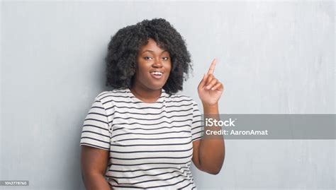 젊은 아프리카계 미국인 플러스 크기 여자 성공적인 아이디어와 손가락 가리키는 회색 그런 지 벽에 종료 하 고 행복 번호
